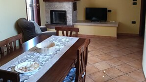 Uma área de refeições com mesa e cadeiras de madeira, lareira, televisão e piso de azulejos.