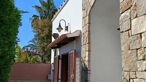 Um edifício de pedra com fachada branca, uma pequena janela com persianas castanhas e um arco de pedra.