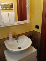Casa de banho com lavatório branco, espelho e suporte para toalhas.