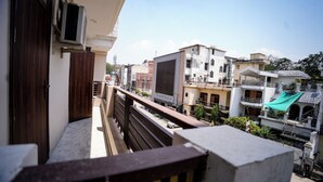 Uma varanda com vista para edifícios próximos, uma porta de madeira e um aparelho de ar condicionado.