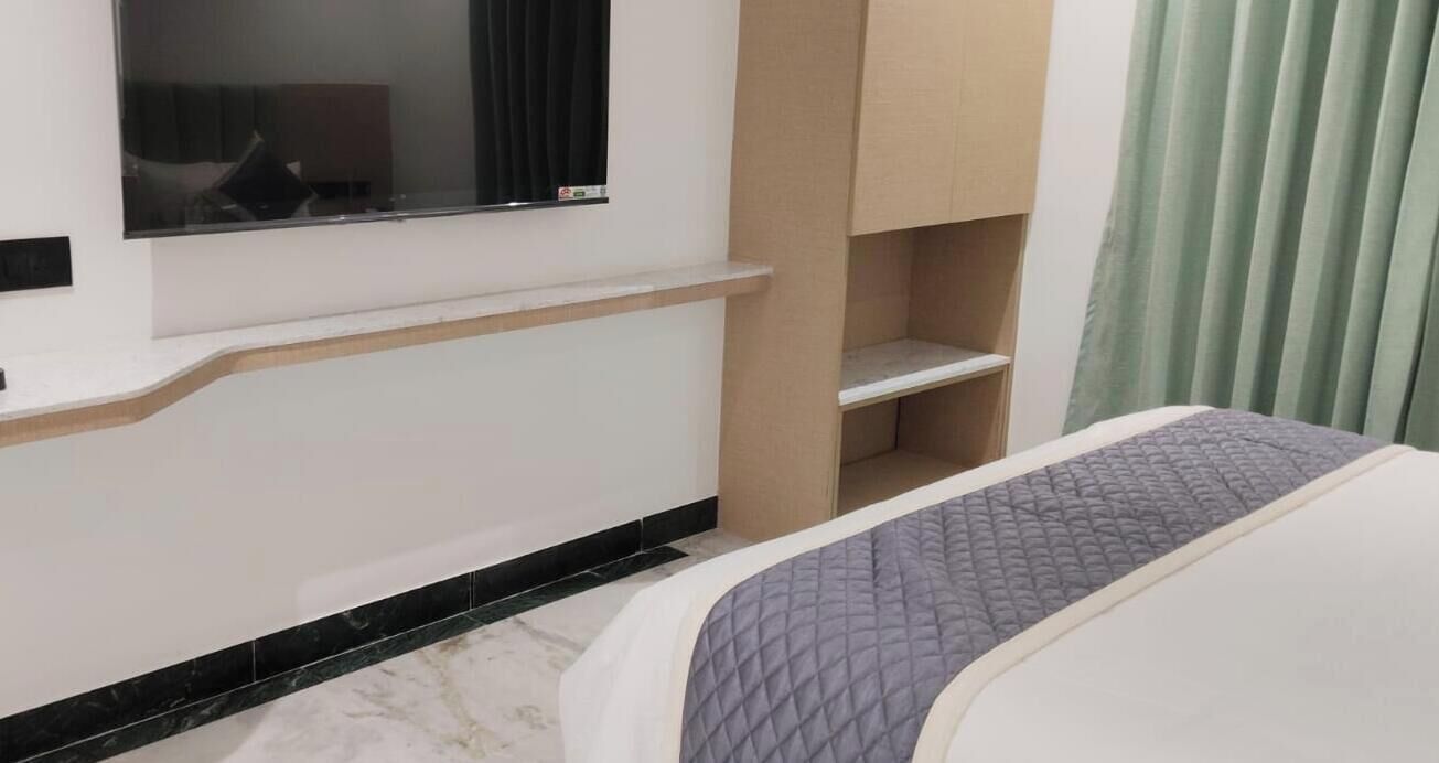 Quarto de hotel com uma cama, uma televisão na parede, uma estante e uma cortina.