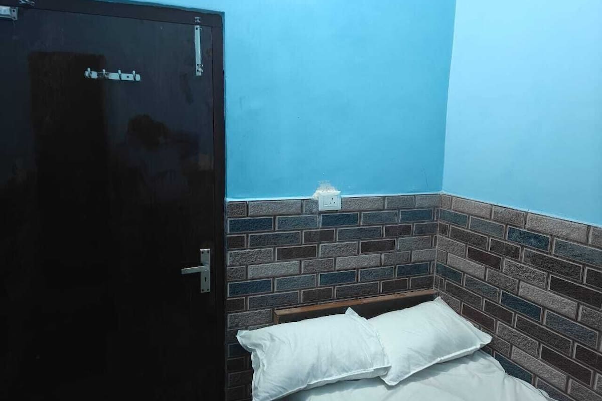 Um quarto pequeno com uma cama, uma porta e uma parede com padrão de tijolos.