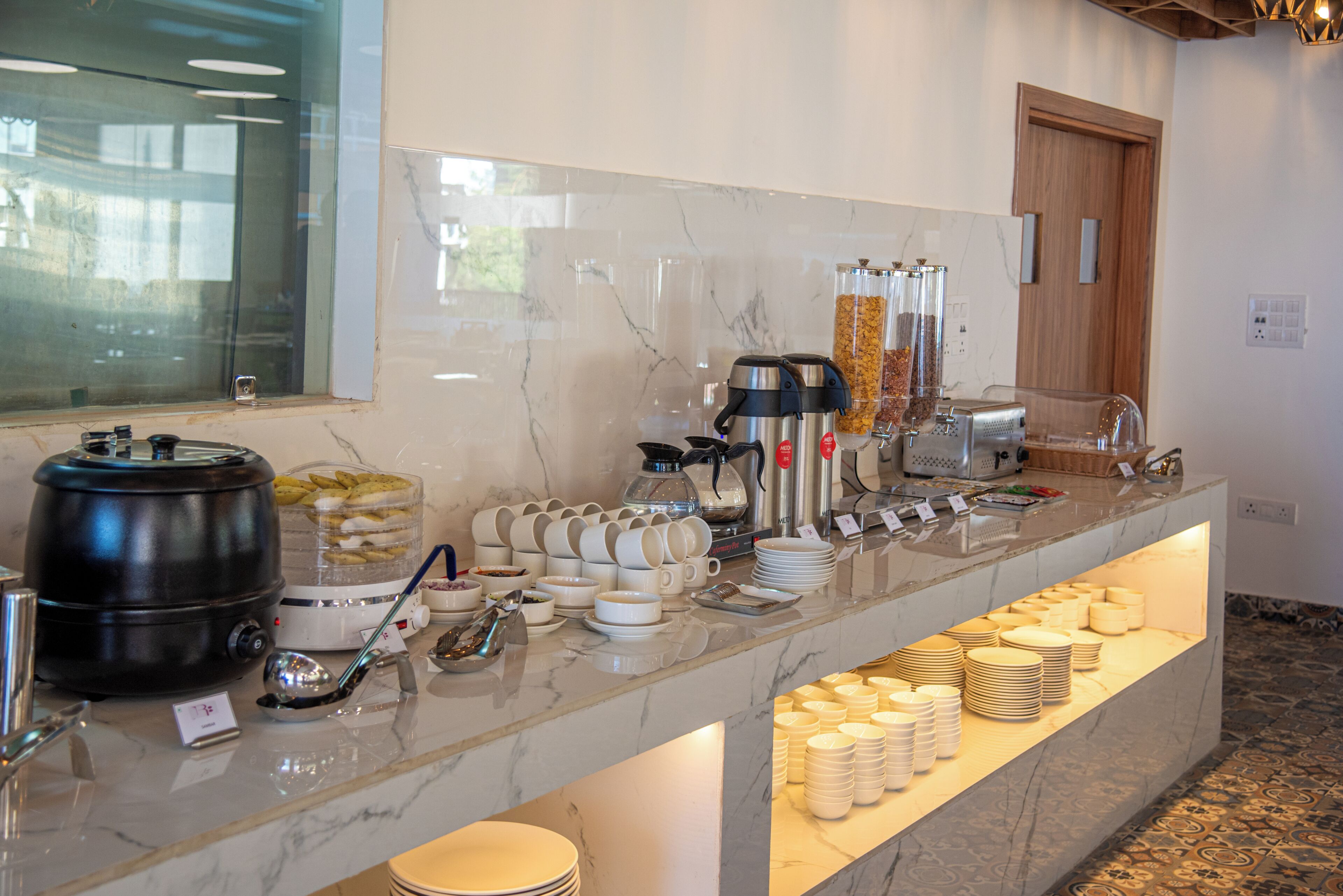 Disposição de buffet com diversos recipientes de comida, utensílios e um espaço para café.