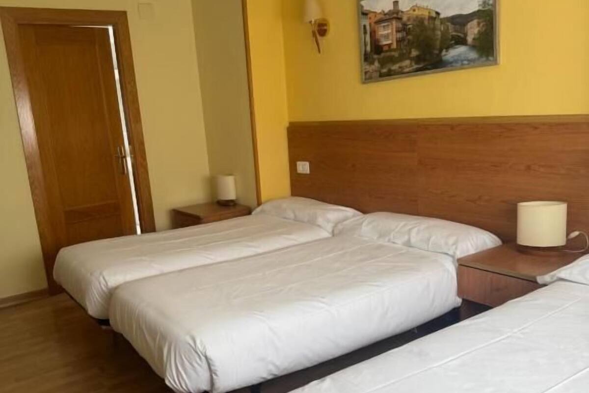 Quarto de hotel com duas camas, piso de madeira, parede amarela e uma pintura.