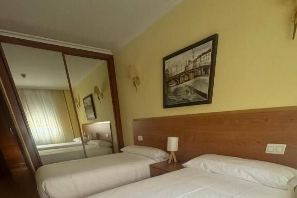 Quarto de hotel com duas camas, uma cabeceira de madeira, um quadro na parede e um espelho.