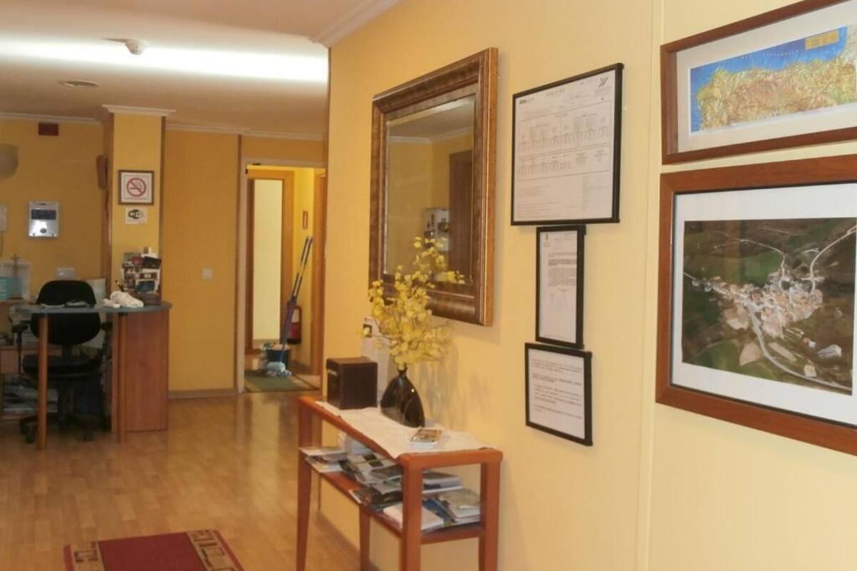 Quarto com escrivaninha de madeira, vaso com flores, quadros nas paredes e um espelho.