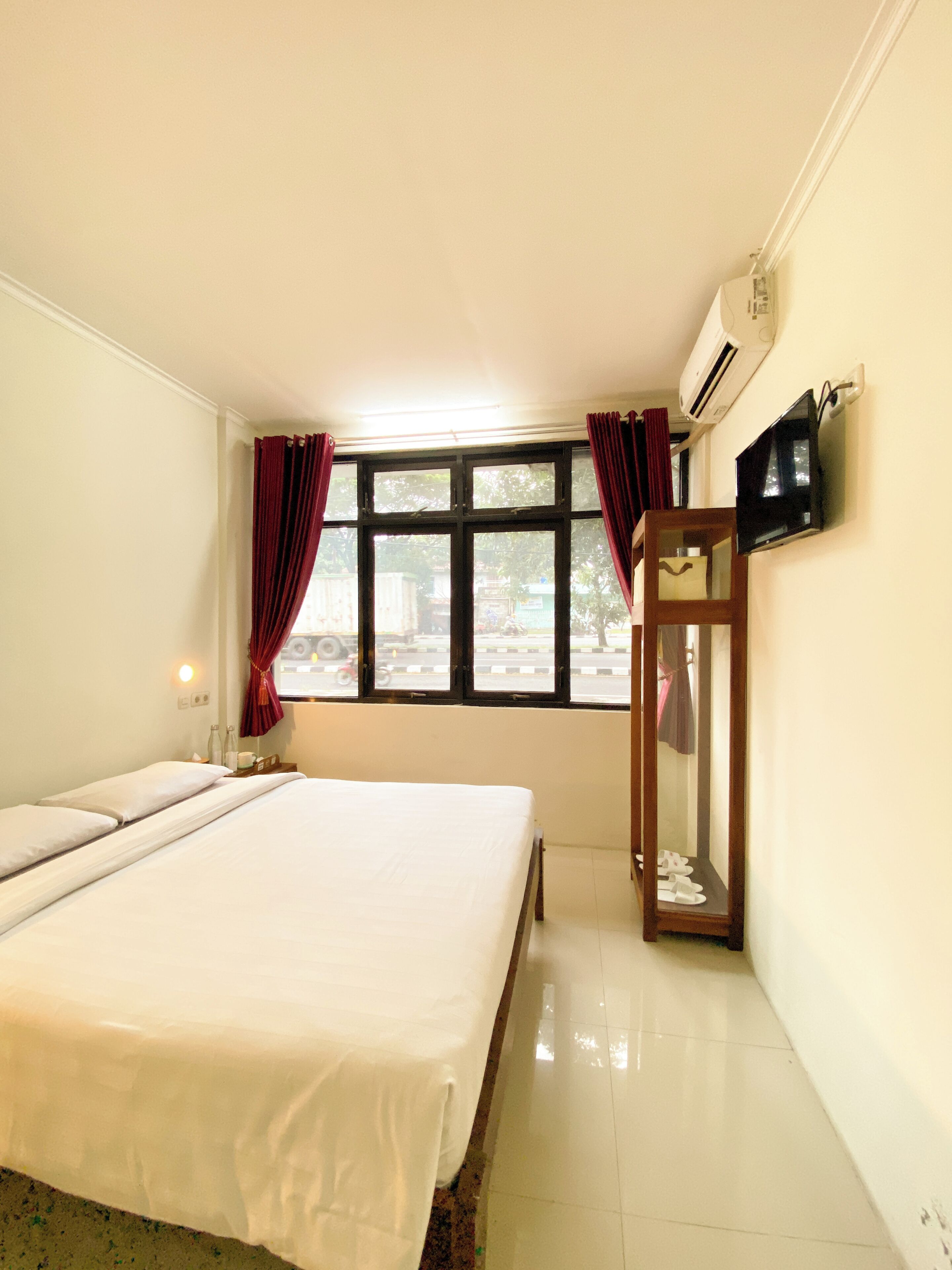 Quarto com cama, janela com cortinas, televisão fixada na parede e espelho.