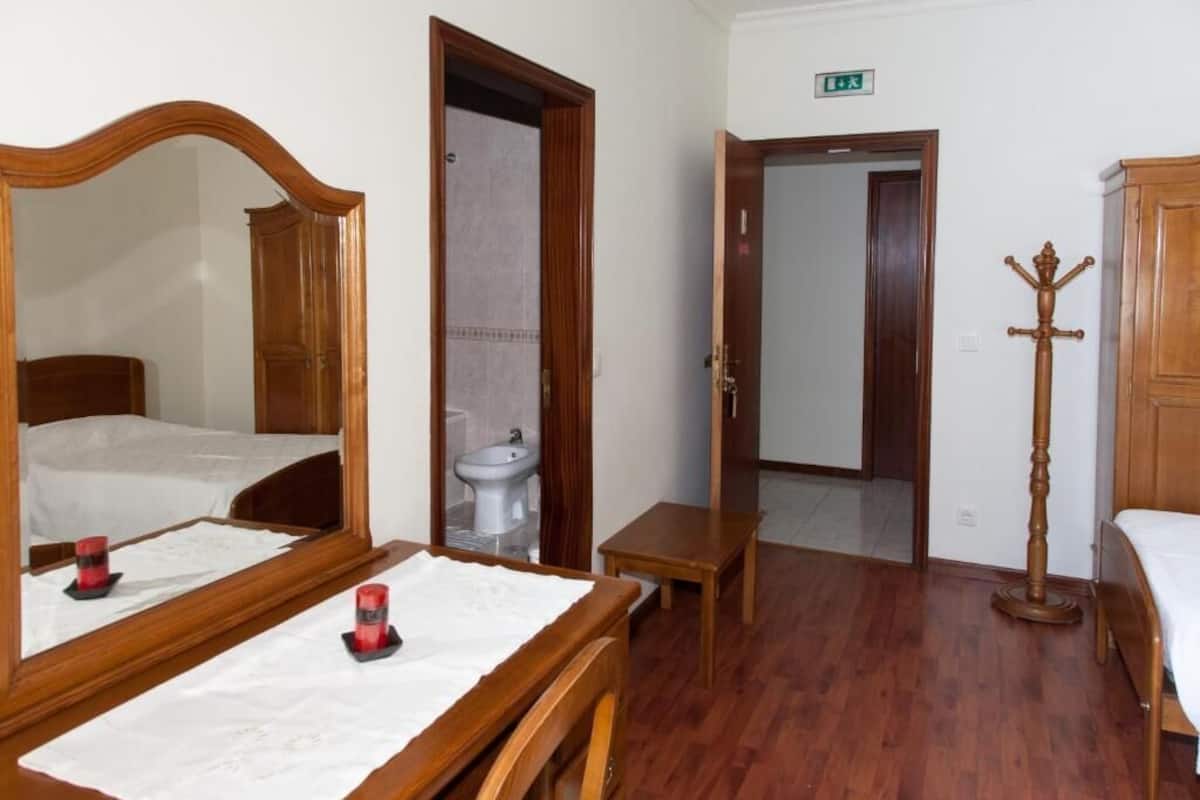 Quarto de hotel com cama de madeira, um espelho grande, mesa de cabeceira com velas, piso de madeira e um cabideiro.