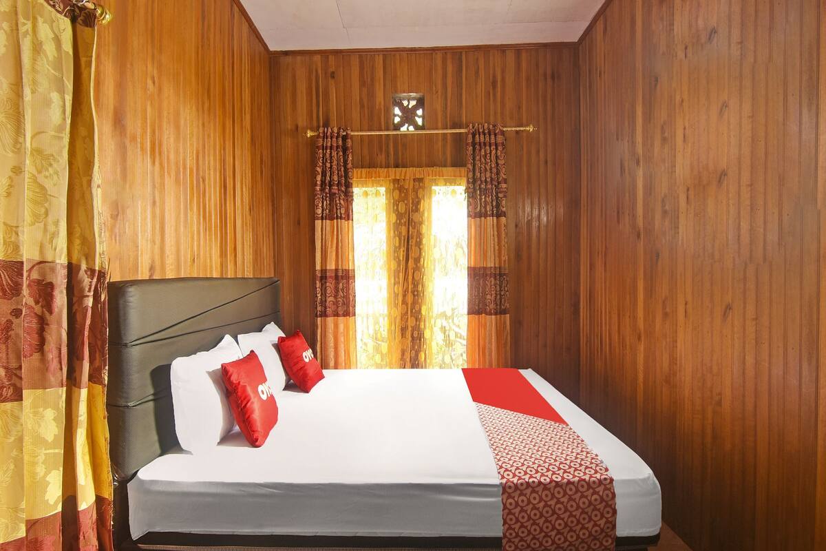 Quarto com painéis de madeira, uma cama, cortinas e uma janela.