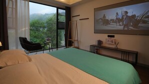 Quarto de hotel moderno com uma cama grande, uma mesa, uma cadeira, uma televisão e vista para o exterior.