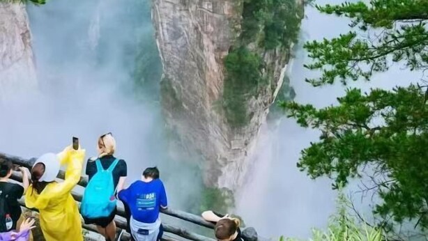Um grupo de pessoas em uma plataforma de observação, com um penhasco íngreme e fundo com névoa.