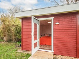 Uma cabana de madeira vermelha com uma cama de solteiro, um pequeno alpendre e uma porta que dá para o quarto.