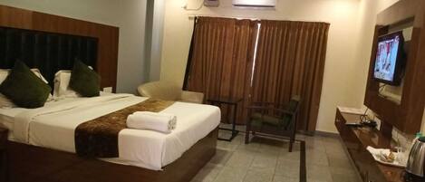 Quarto de hotel com cama, escrivaninha, cadeira, televisão e ar condicionado.