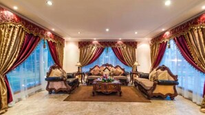 Um quarto luxuoso com mobiliário requintado, janelas amplas e um candelabro.