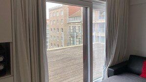 Quarto de hotel com uma janela grande, uma cama, um sofá de couro preto e um termostato na parede.