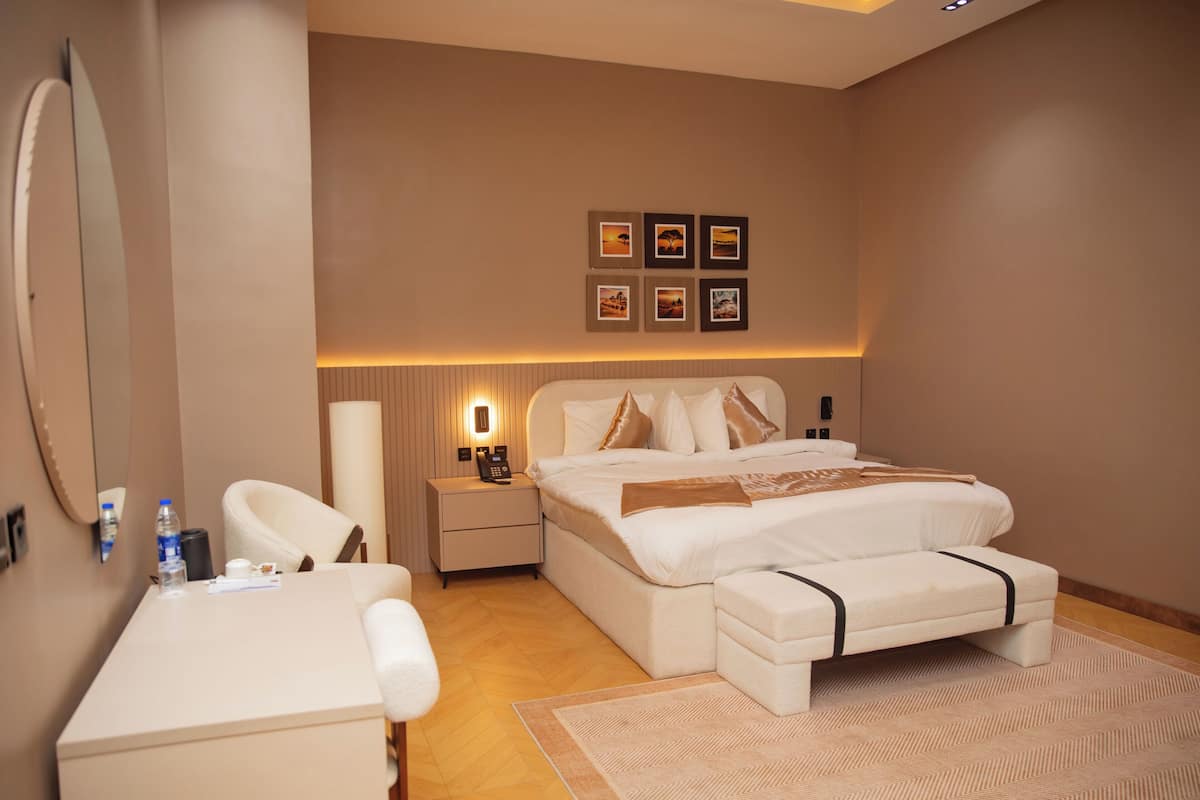 Quarto de hotel moderno com cama, mesa de cabeceira, luminária e uma obra de arte na parede.