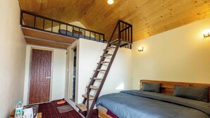 Quarto com teto de madeira, cama com roupa de cama cinzenta, escada de madeira para um mezanino e uma porta.