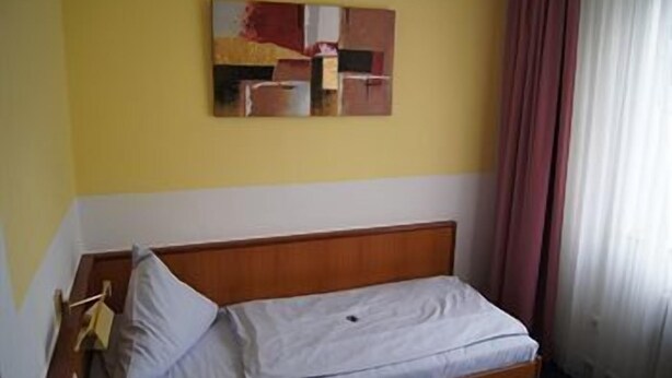 Uma cama de solteiro com cabeceira de madeira, um travesseiro e uma pintura abstrata pendurada na parede.