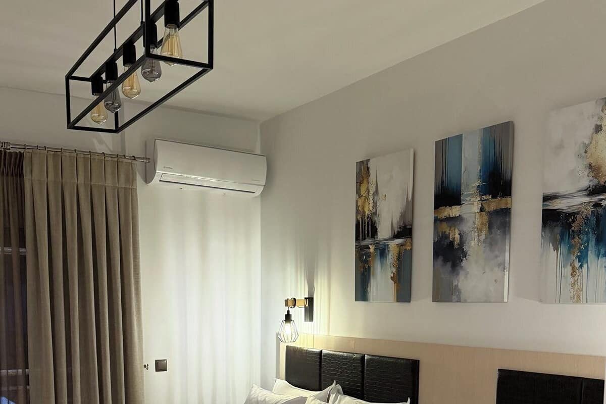 Quarto de hotel com duas camas, cortinas bege, luminária moderna e obras de arte na parede.