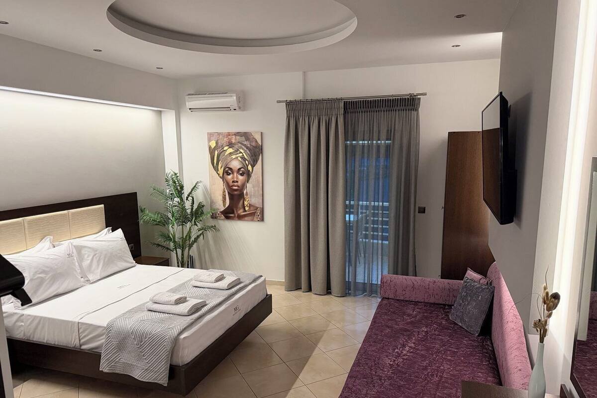Quarto de hotel moderno com cama, sofá, televisão e janela com cortinas.