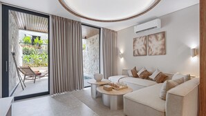 Quarto de hotel moderno com sofá, mesa de centro, jogo de xadrez e vista para o jardim.