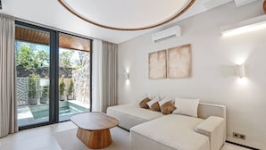 Uma sala de estar moderna com um sofá, uma mesa de centro e um vão de vidro que dá para uma área externa.