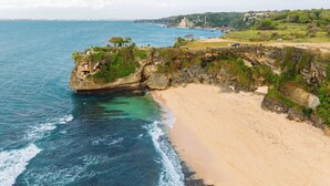 Paisagem costeira com uma praia arenosa, falésias rochosas e vista do mar.
