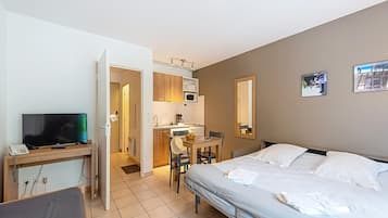 Quarto de hotel com cama, escrivaninha com televisão, cozinha compacta e banheiro.