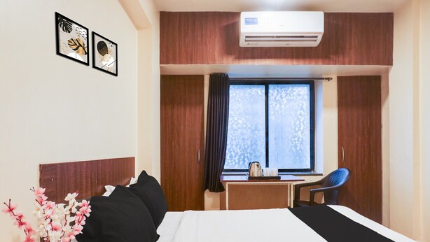 Quarto de hotel com cama, escrivaninha, cadeira, ar condicionado e janela com cortinas.