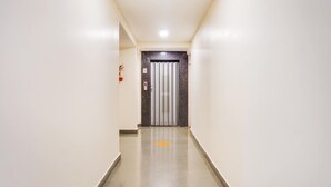 Um corredor com uma porta no final, um alarme de incêndio na parede e um chão com uma seta indicativa.
