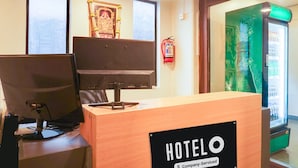 Balcão de recepção de hotel com computador, extintor de incêndio e frigorífico.