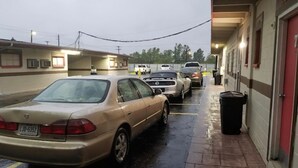 Um estacionamento com carros, um edifício com porta vermelha e uma lixeira.