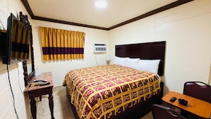 Quarto de hotel com cama, escrivaninha, cadeira, televisão, janela com cortinas e ar condicionado.