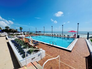 Piscina com vista para a praia, rodeada por espreguiçadeiras e guarda-sóis.