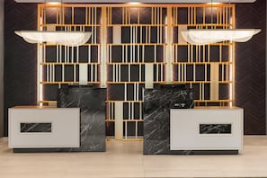 Uma área de recepção com design moderno, destacando uma parede com padrão escuro, luminária geométrica e balcões de mármore.