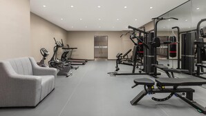 Academia moderna com equipamentos de ginástica, um sofá e um espelho grande.