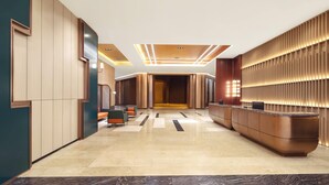 Um saguão de hotel moderno com balcão de recepção, área de estar e corredor que dá para os quartos.