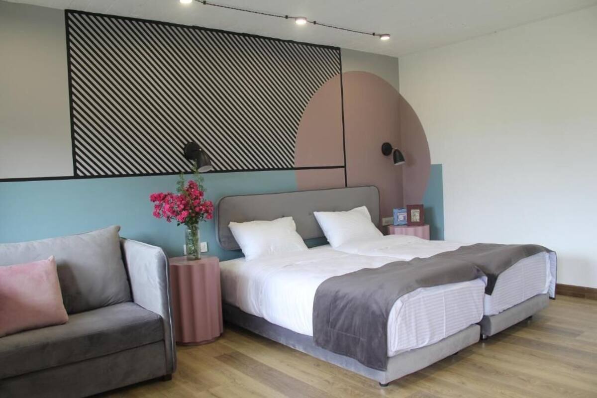 Quarto com cama, sofá, luminária na parede e painel decorativo.