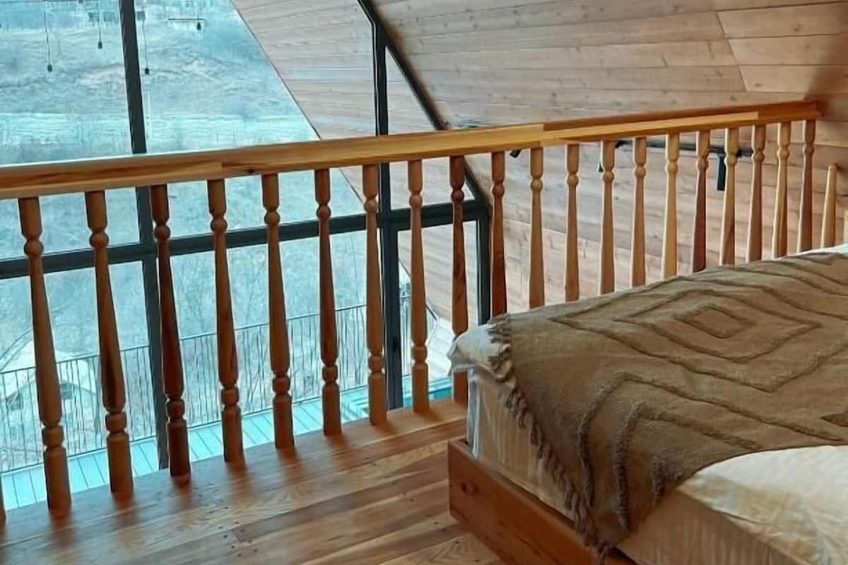 Quarto com teto e corrimão de madeira, e uma grande janela.