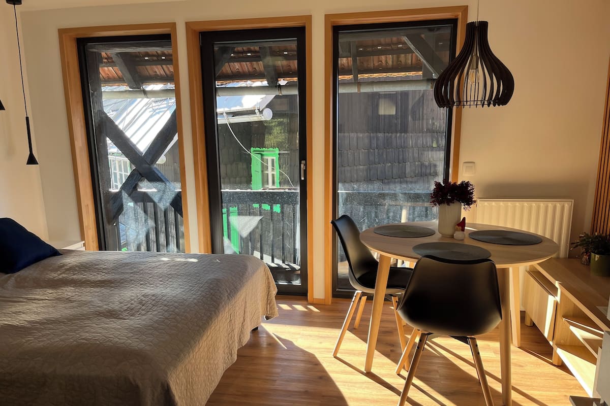 Quarto com cama, mesa de jantar com cadeiras, planta em vaso e radiador.