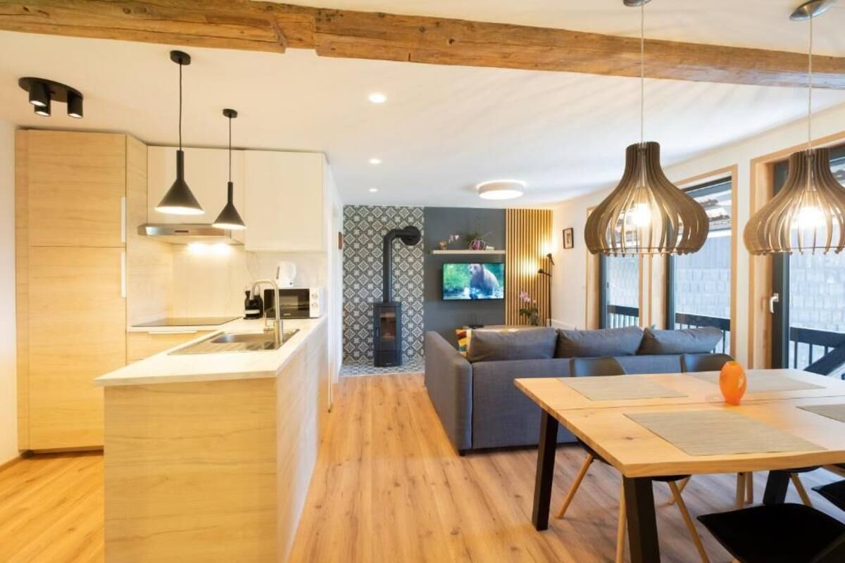 Uma cozinha moderna com armários de madeira, uma ilha central, luminárias pendentes, um sofá e uma mesa de jantar com um vaso.