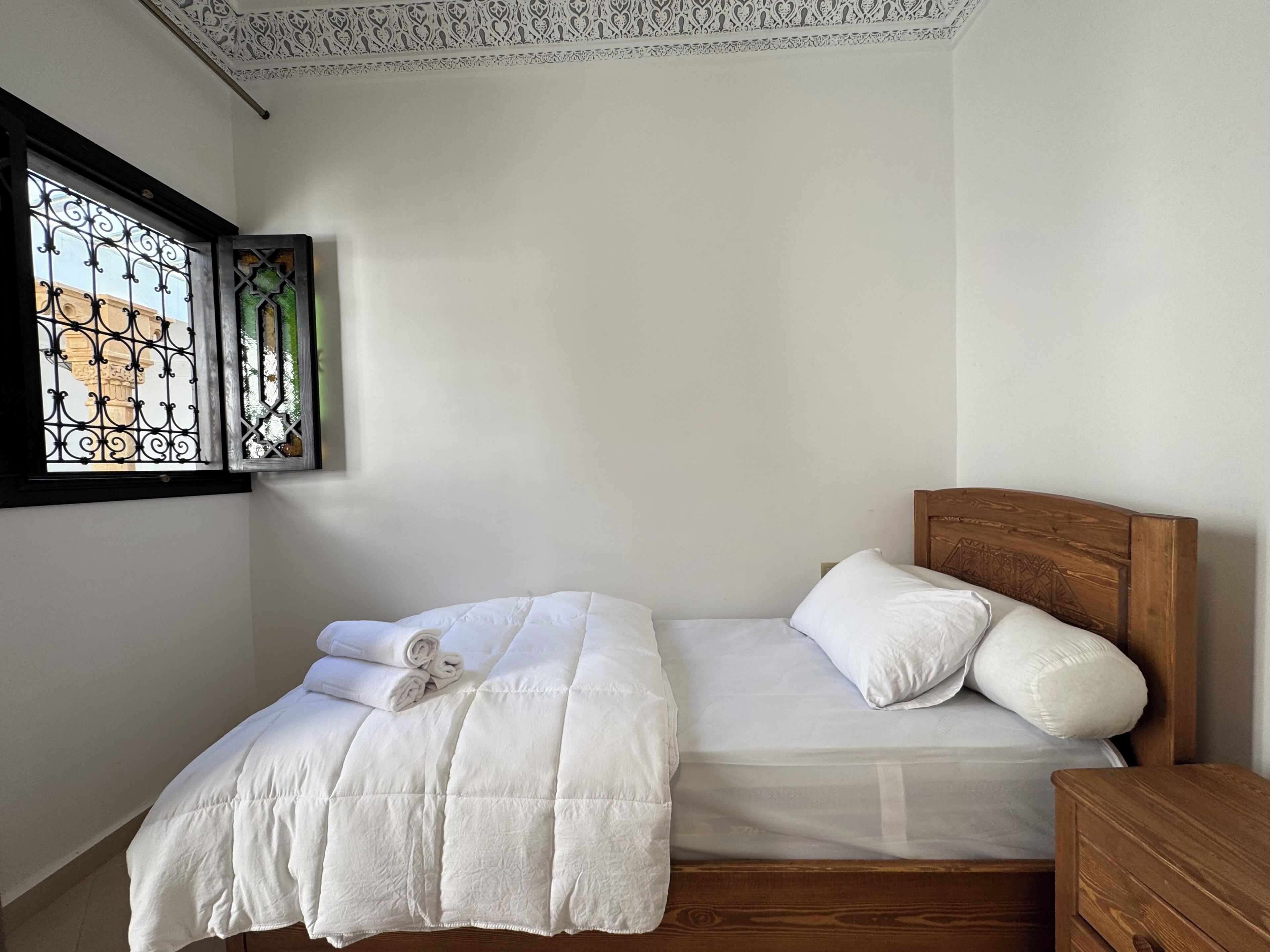 Quarto com cabeceira de madeira, colcha branca e toalha enrolada na cama.