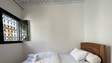 Quarto com cabeceira de madeira, colcha branca e toalha enrolada na cama.