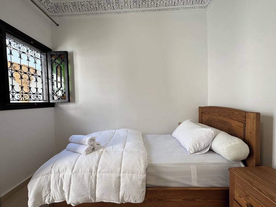 Quarto com cabeceira de madeira, colcha branca e toalha enrolada na cama.