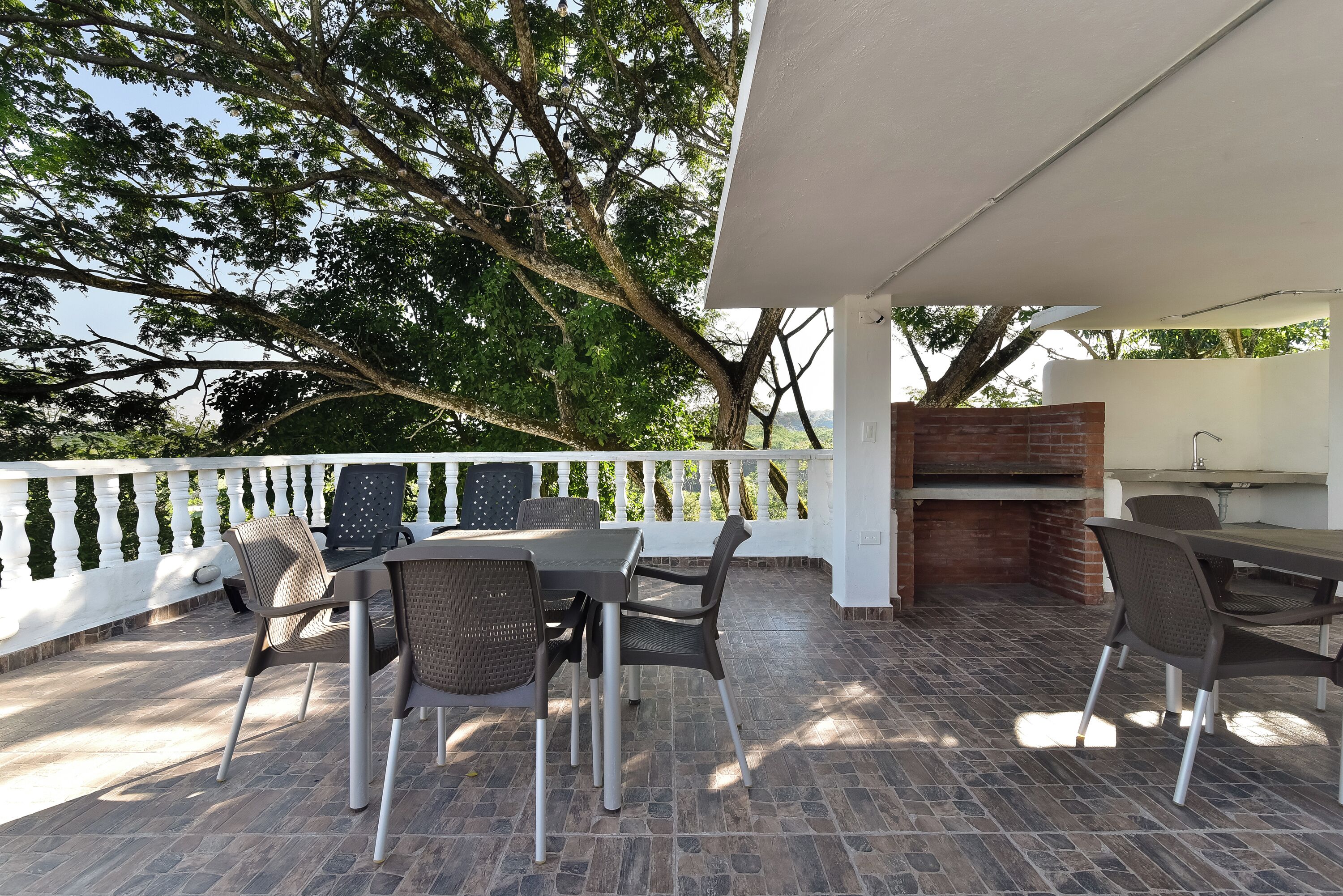 Um pátio ao ar livre com mesa, cadeiras, forno de tijolos e corrimão branco.