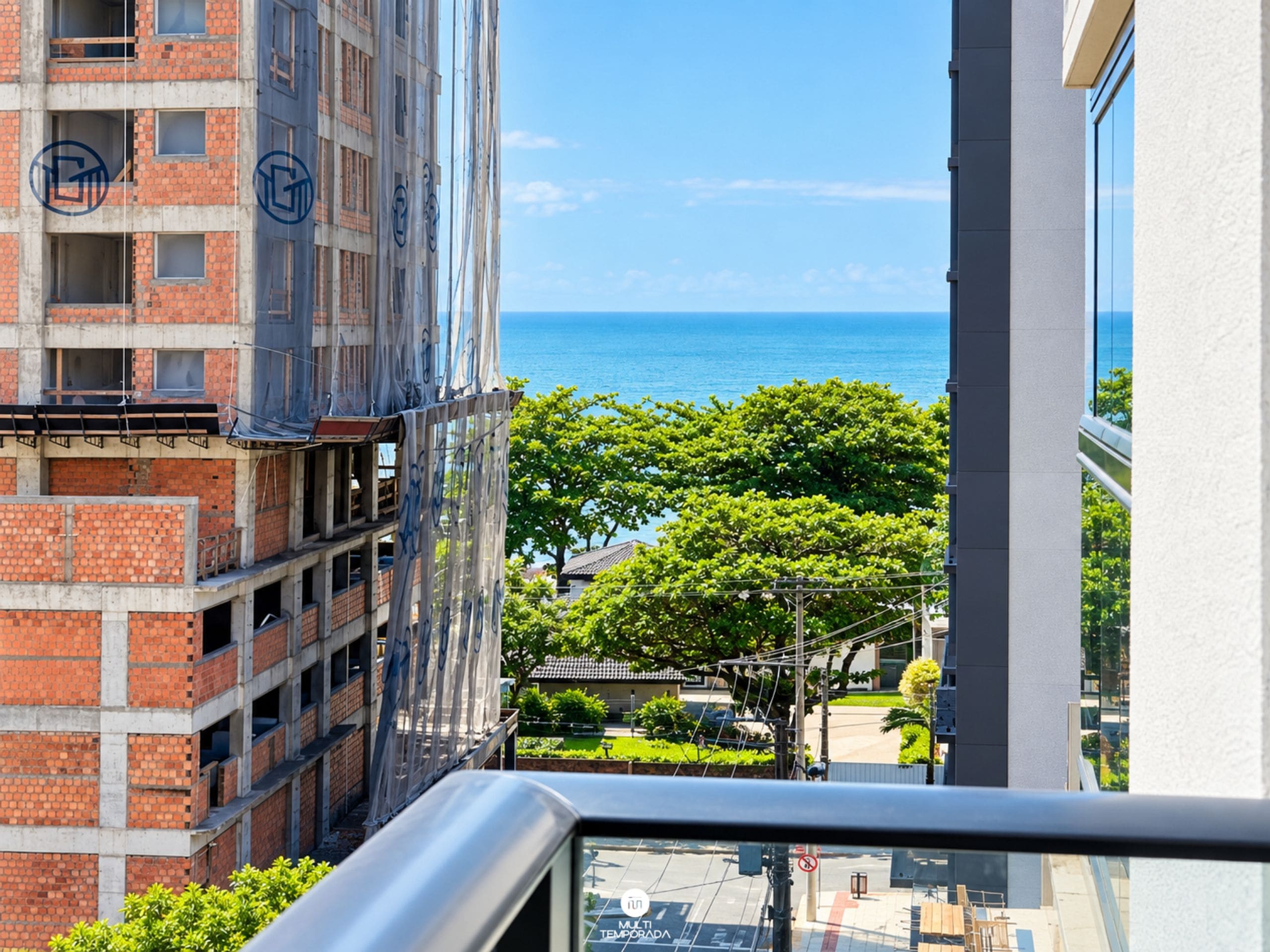 Um edifício alto com vista para o mar, uma varanda e céu claro.