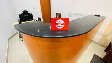 Bancada de recepção com um sinal vermelho 'Accepted Here', um alto-falante preto e uma porta de madeira ao fundo.