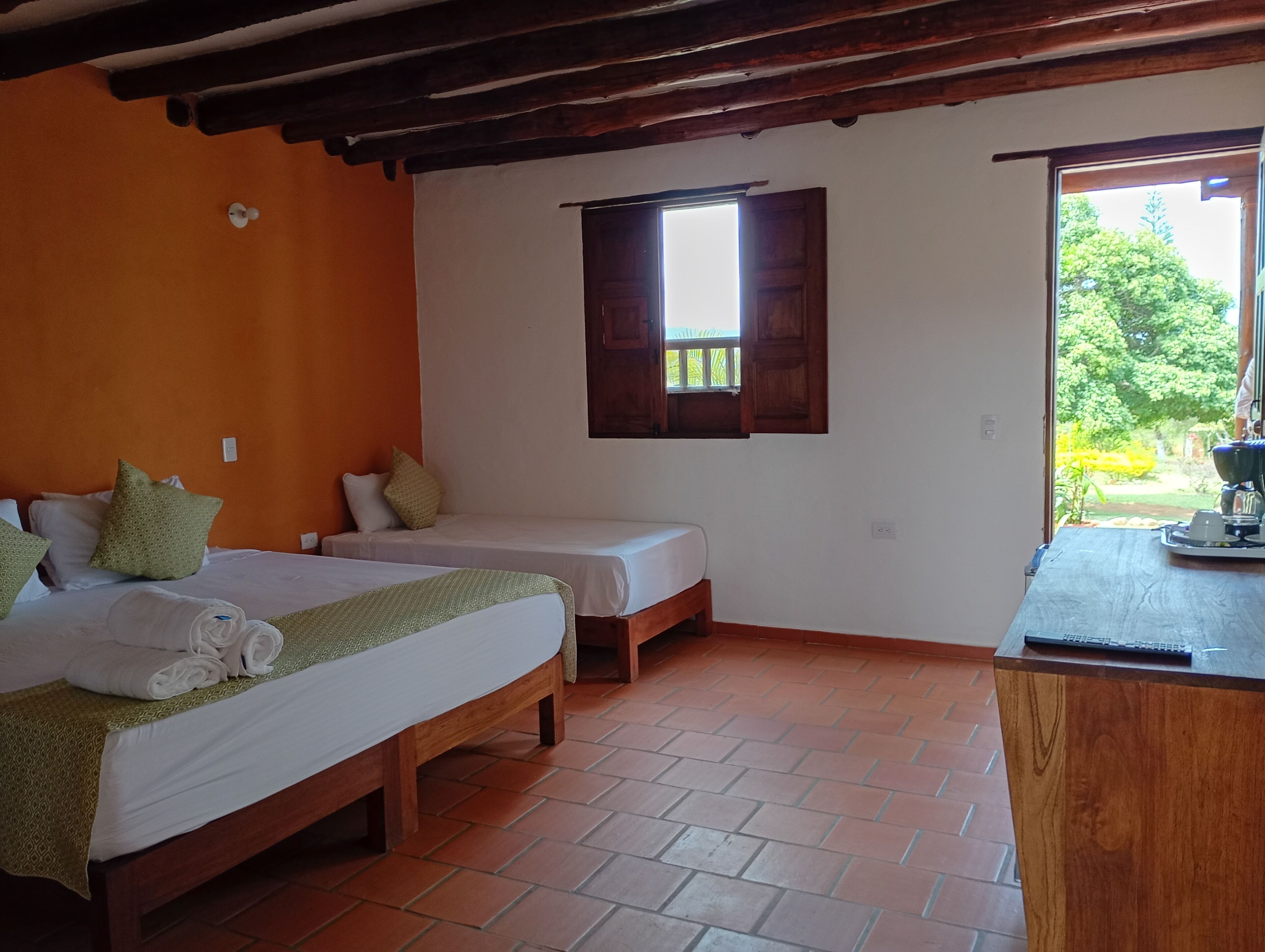 Quarto com duas camas, teto de madeira, janela com vista para vegetação e chão de azulejos.