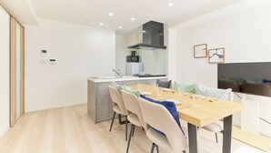 Cozinha moderna com ilha central, área de jantar com mesa e cadeiras de madeira, e televisão de tela plana fixada na parede.