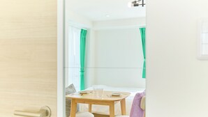Um quarto com uma mesa de madeira, duas cadeiras, uma cama e uma janela com cortinas.